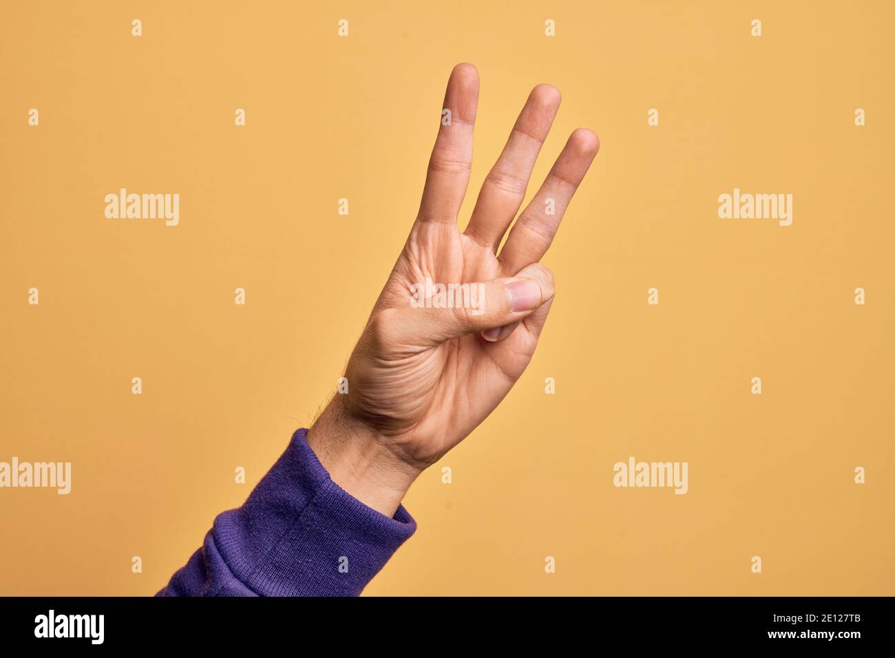 Hand of caucasian young man showing fingers over isolated yellow background counting number 3 ...