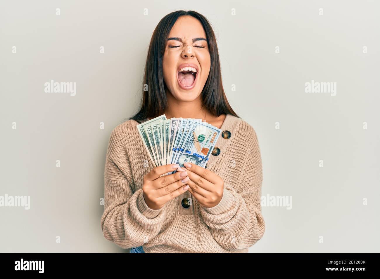 Young beautiful hispanic girl holding dollars angry and mad screaming ...