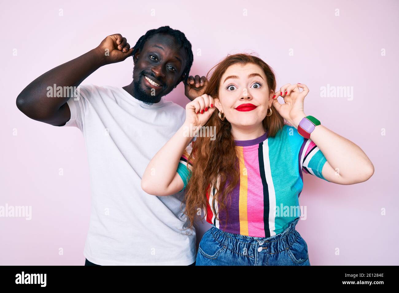 Interracial couple wearing casual clothes smiling pulling ears with ...