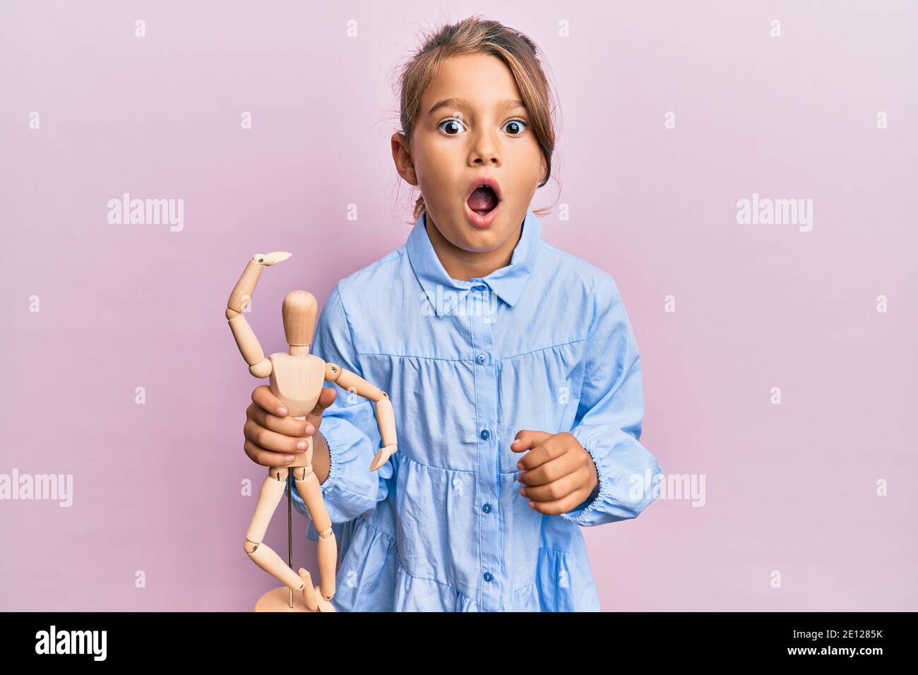 Little beautiful girl holding small wooden manikin scared and amazed ...