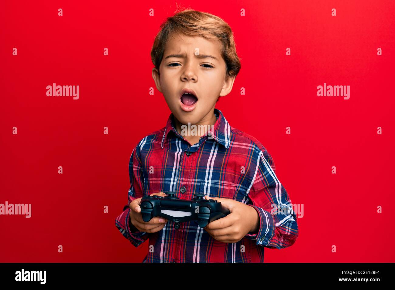 Adorable latin kid playing video game holding controller in shock face ...