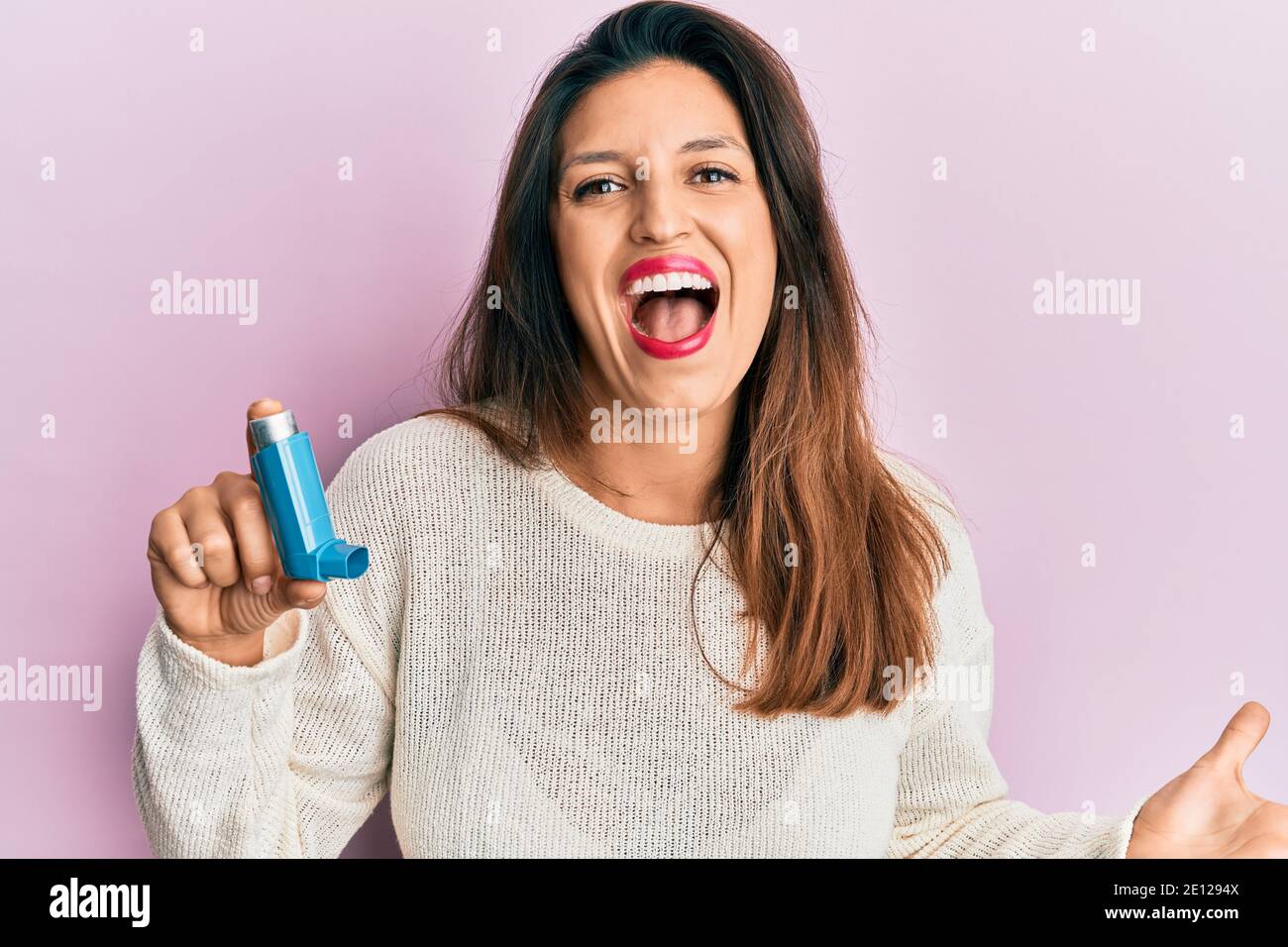 Beautiful hispanic woman holding medical asthma inhaler celebrating ...