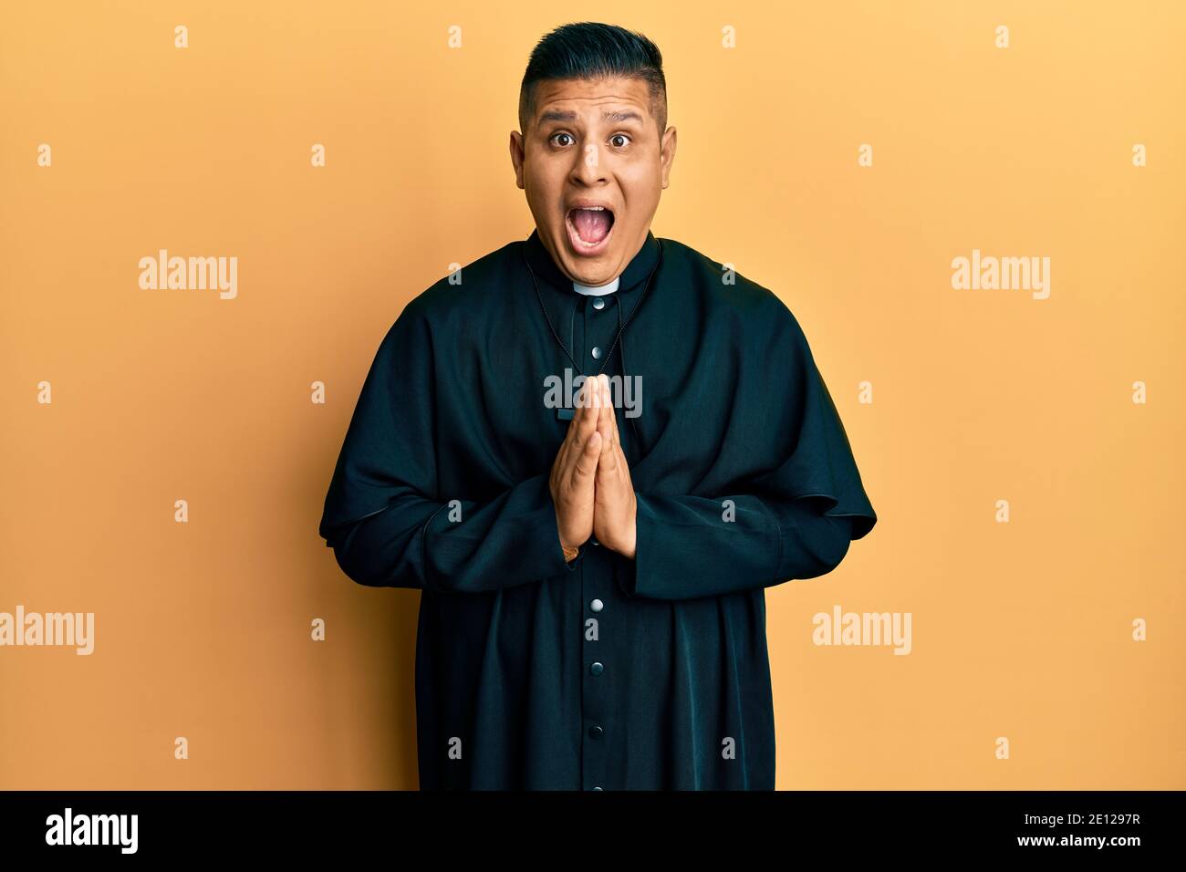 Young latin priest man praying with hands together celebrating crazy ...