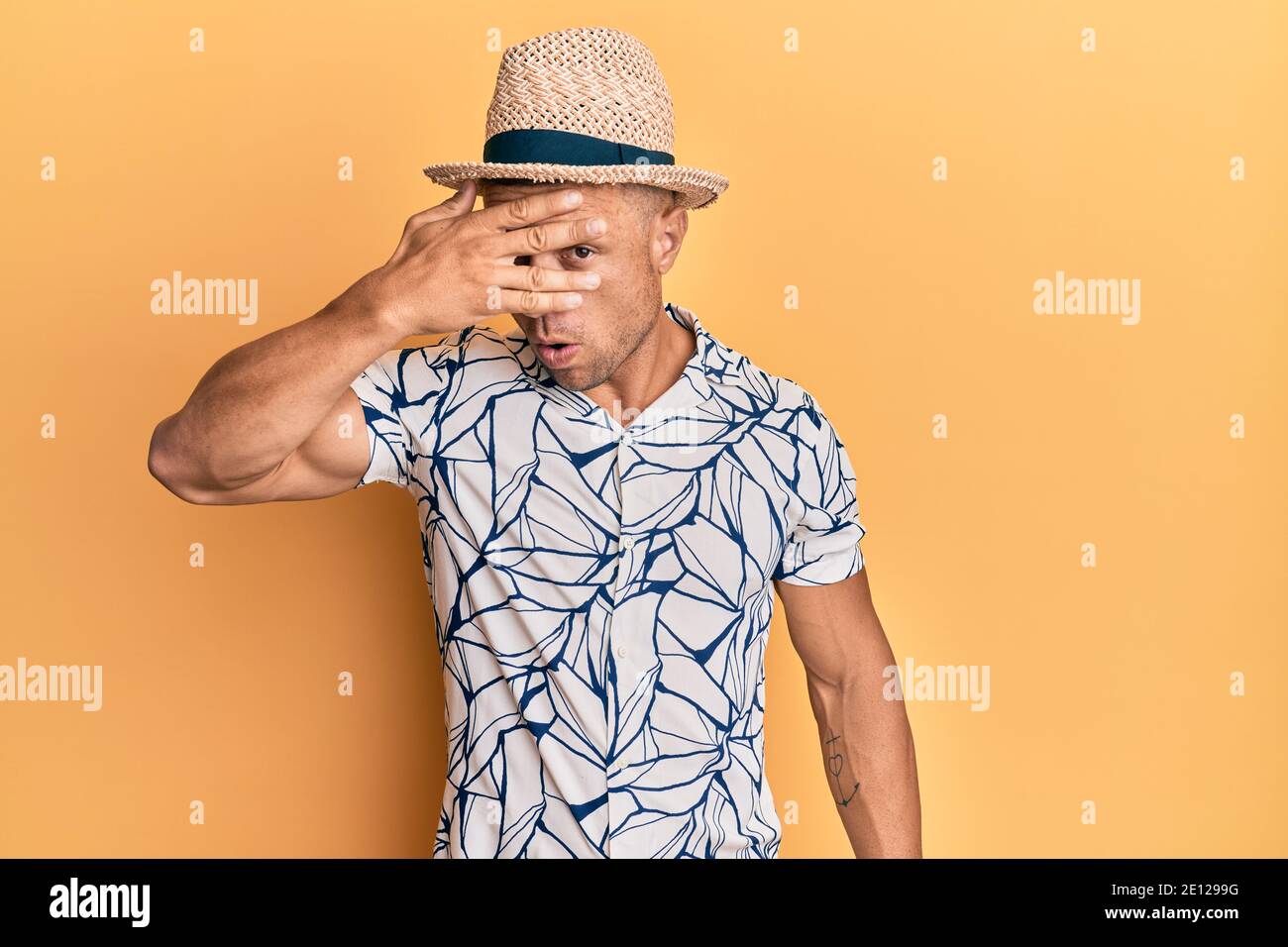 Handsome muscle man wearing summer hat peeking in shock covering face ...