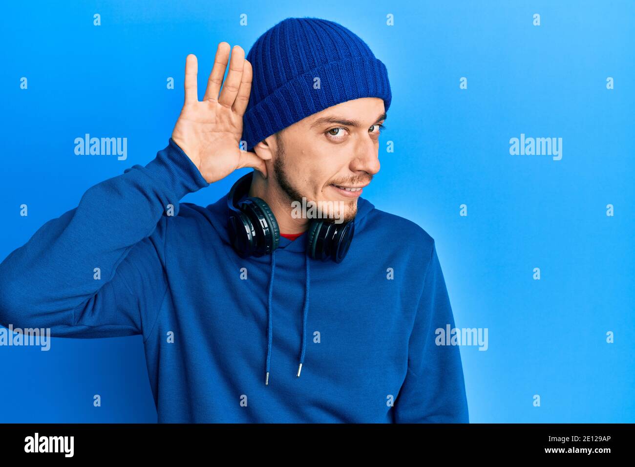 Hispanic young man wearing sweatshirt and headphones smiling with hand ...