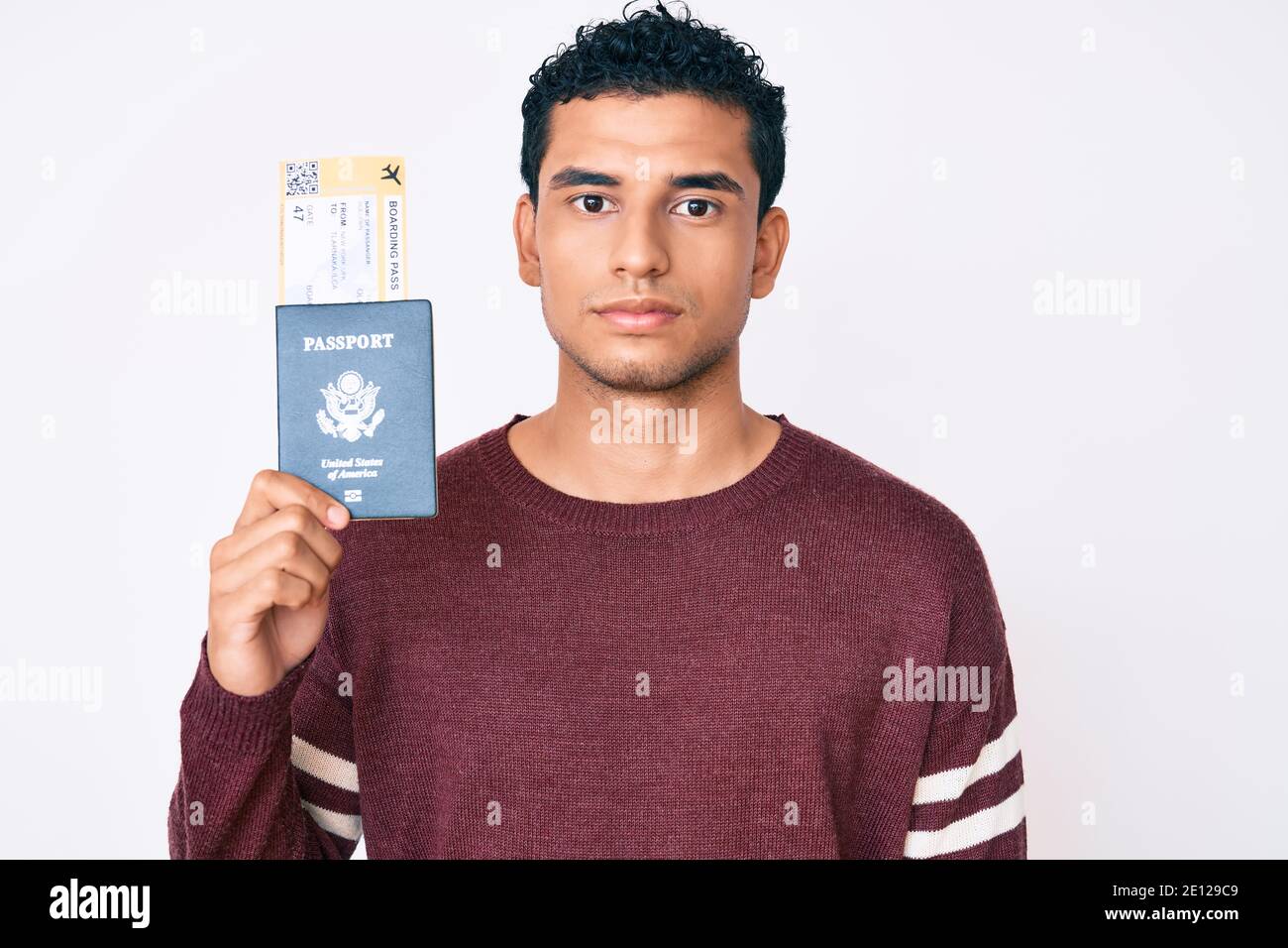 Young handsome hispanic man holding boarding pass and passport thinking ...