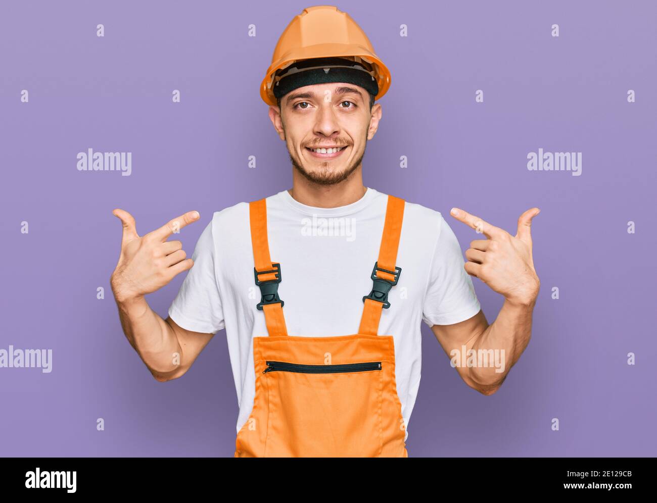 Hispanic young man wearing handyman uniform and safety hardhat looking ...