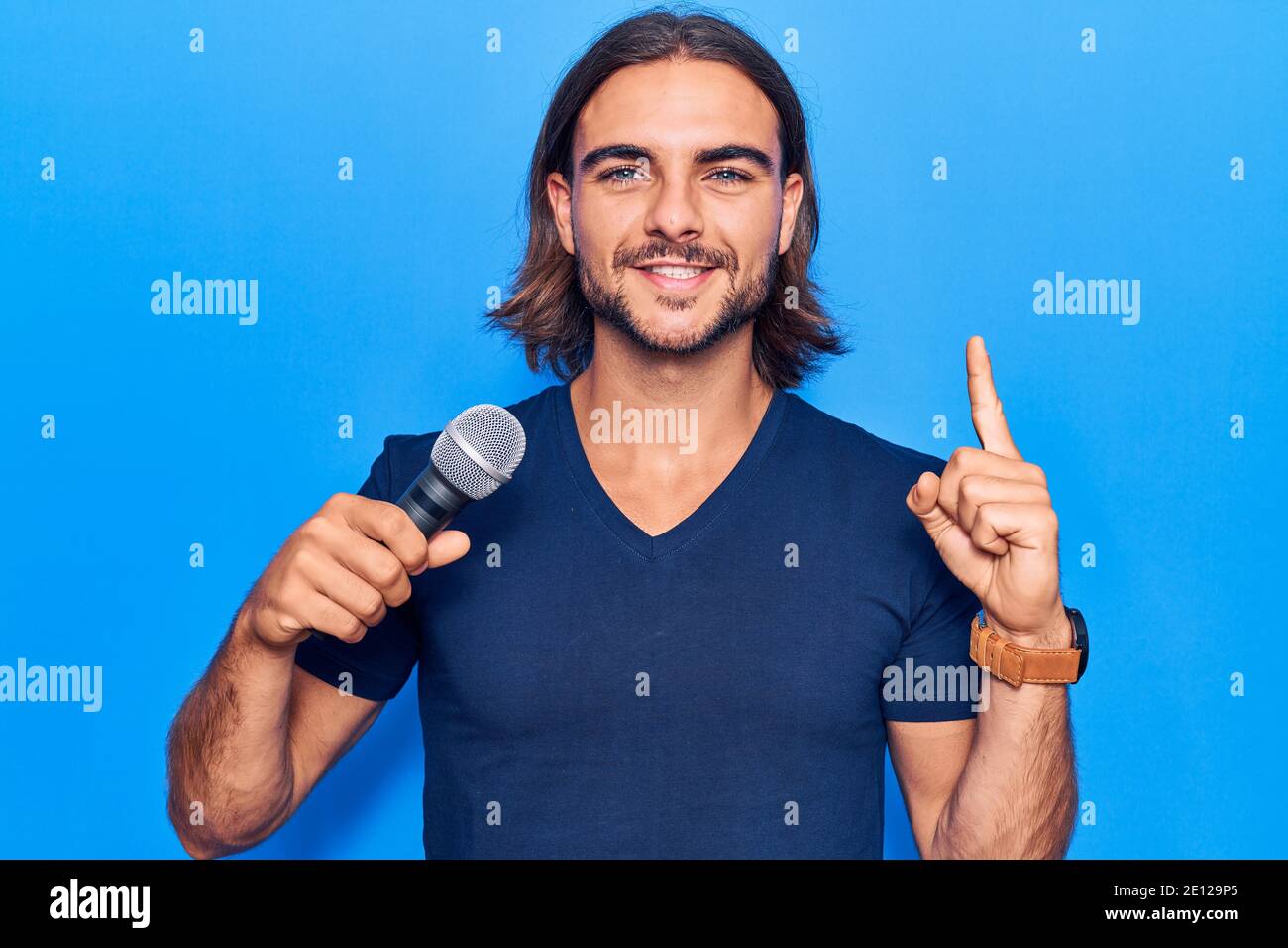 Young handsome man singing song using microphone smiling with an idea ...