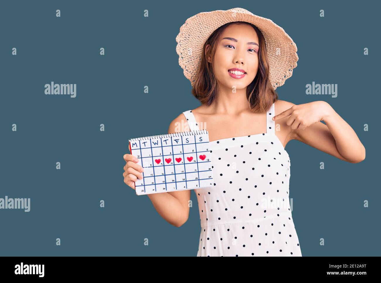 Young beautiful chinese girl wearing summer hat holding heart calendar ...