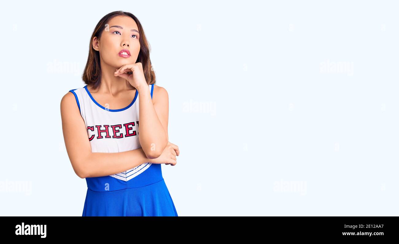 Young beautiful chinese girl wearing cheerleader uniform with hand on ...