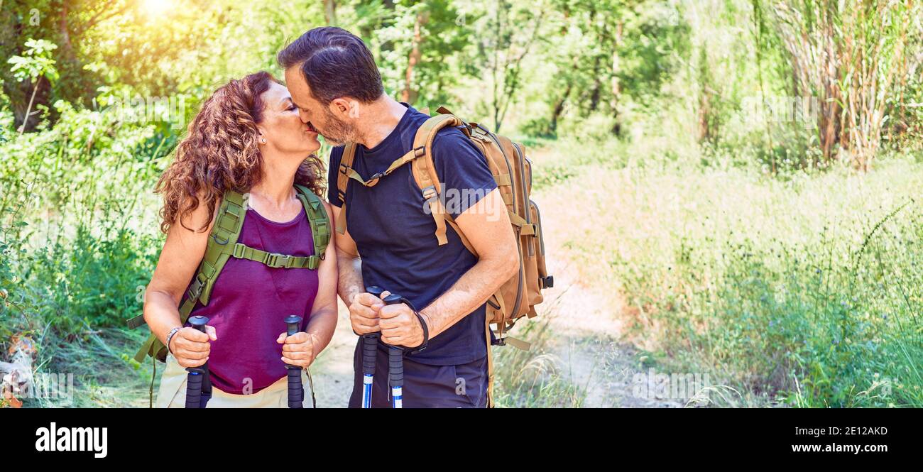 Beautiful couple of hiker wearing backpack kissing. Standing at forest ...