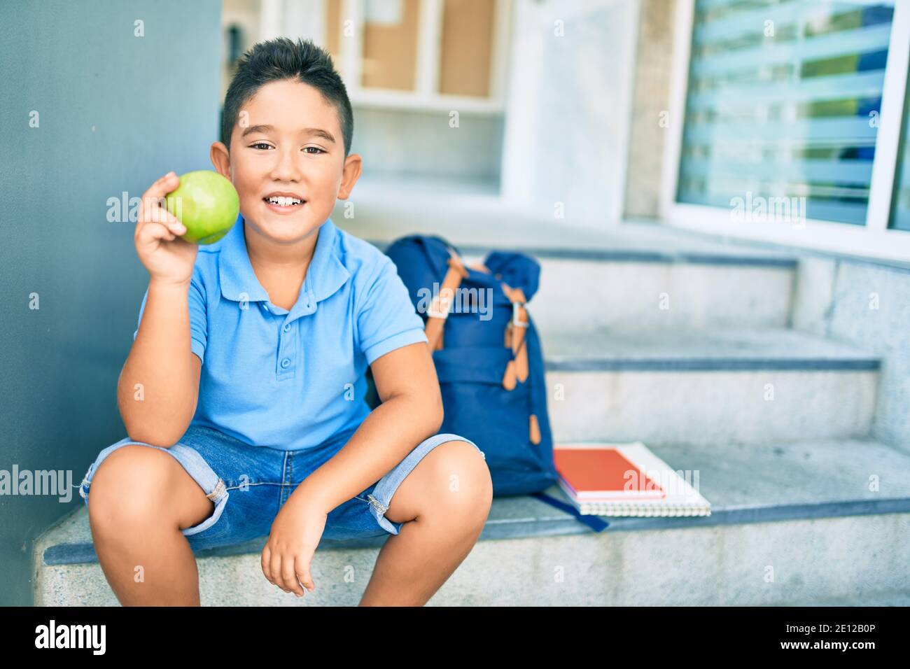 Adorable student boy smiling happy holding green apple sitting on the ...