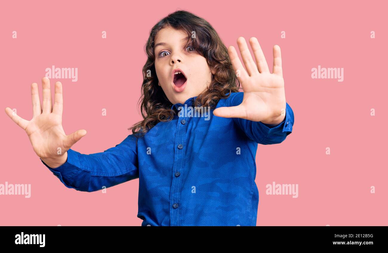 Cute child with long hair wearing casual clothes afraid and terrified ...