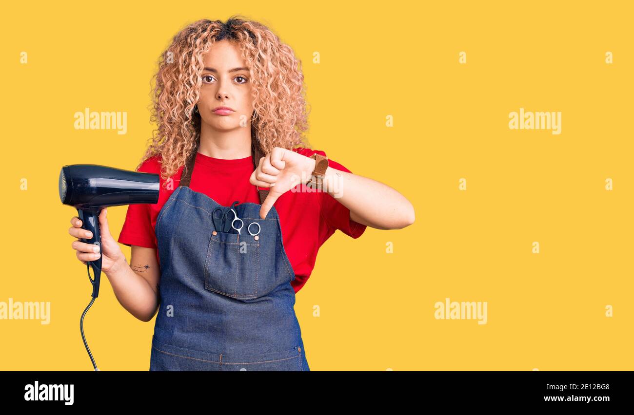 Young blonde woman with curly hair wearing hairdresser apron and ...