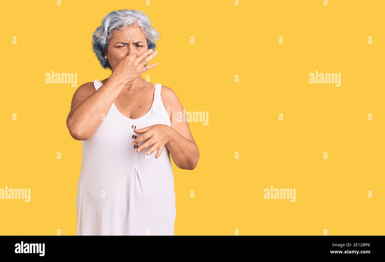 Senior woman with gray hair wearing casual clothes smelling something ...