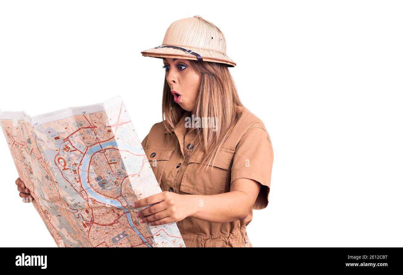 Young beautiful woman wearing explorer hat holding map scared and ...