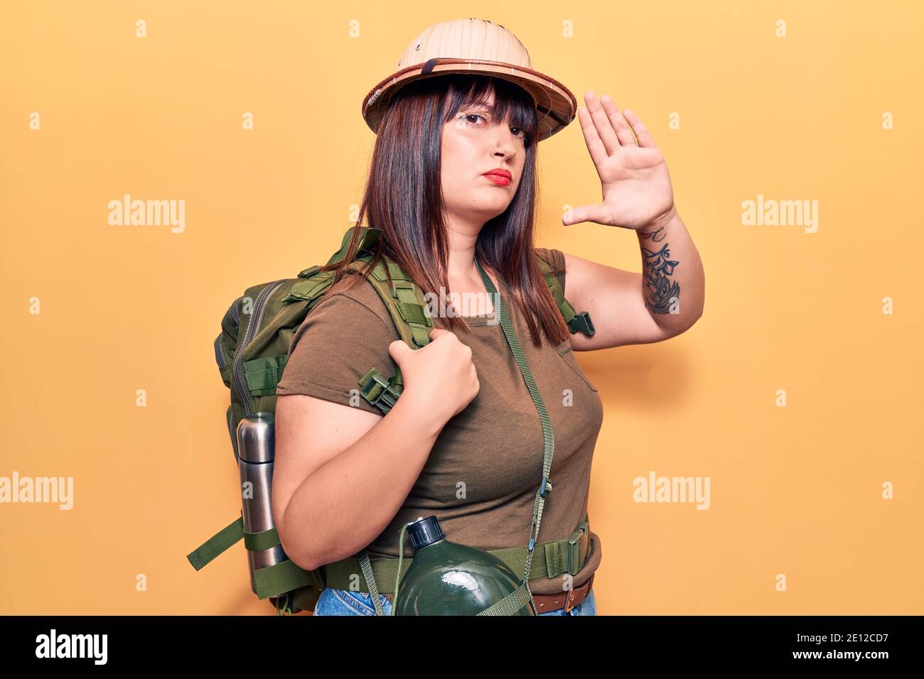Young plus size woman wearing explorer hat and backpack with open hand ...