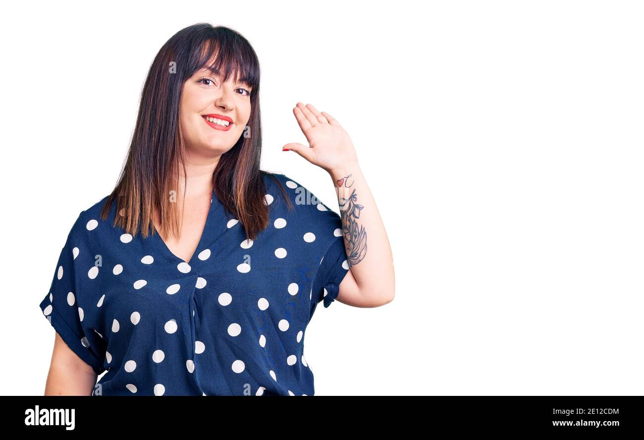 Young plus size woman wearing casual clothes waiving saying hello happy ...