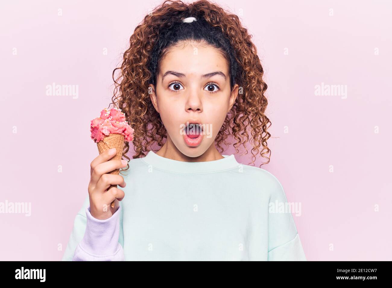 Beautiful kid girl with curly hair holding ice cream scared and amazed ...