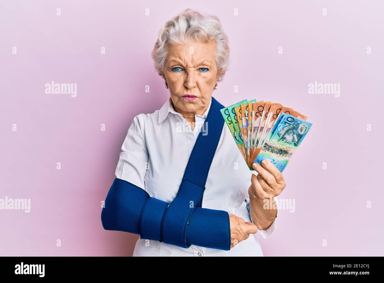 Senior grey-haired woman wearing arm on sling holding australia dollars ...