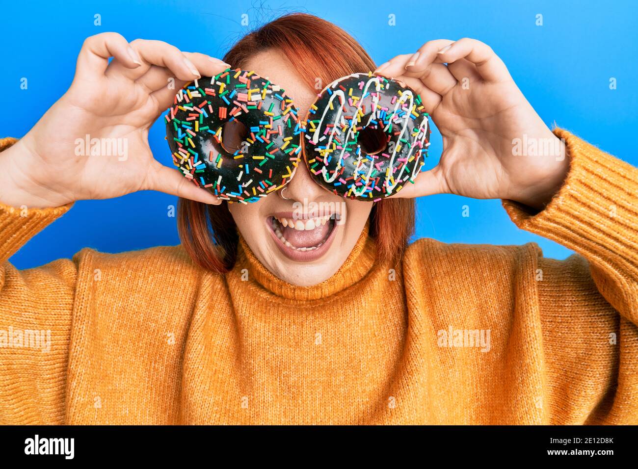 Beautiful redhead woman holding tasty colorful doughnuts on eyes ...