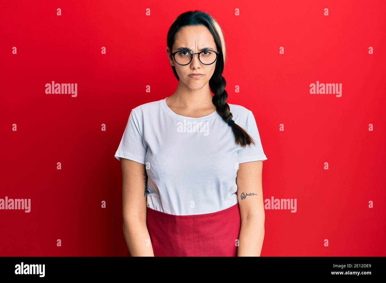 Young hispanic woman wearing professional waitress apron skeptic and ...