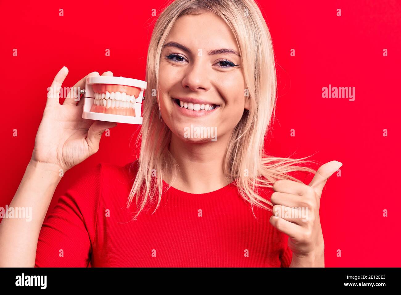 Young beautiful blonde woman holding denture teeth standing over ...