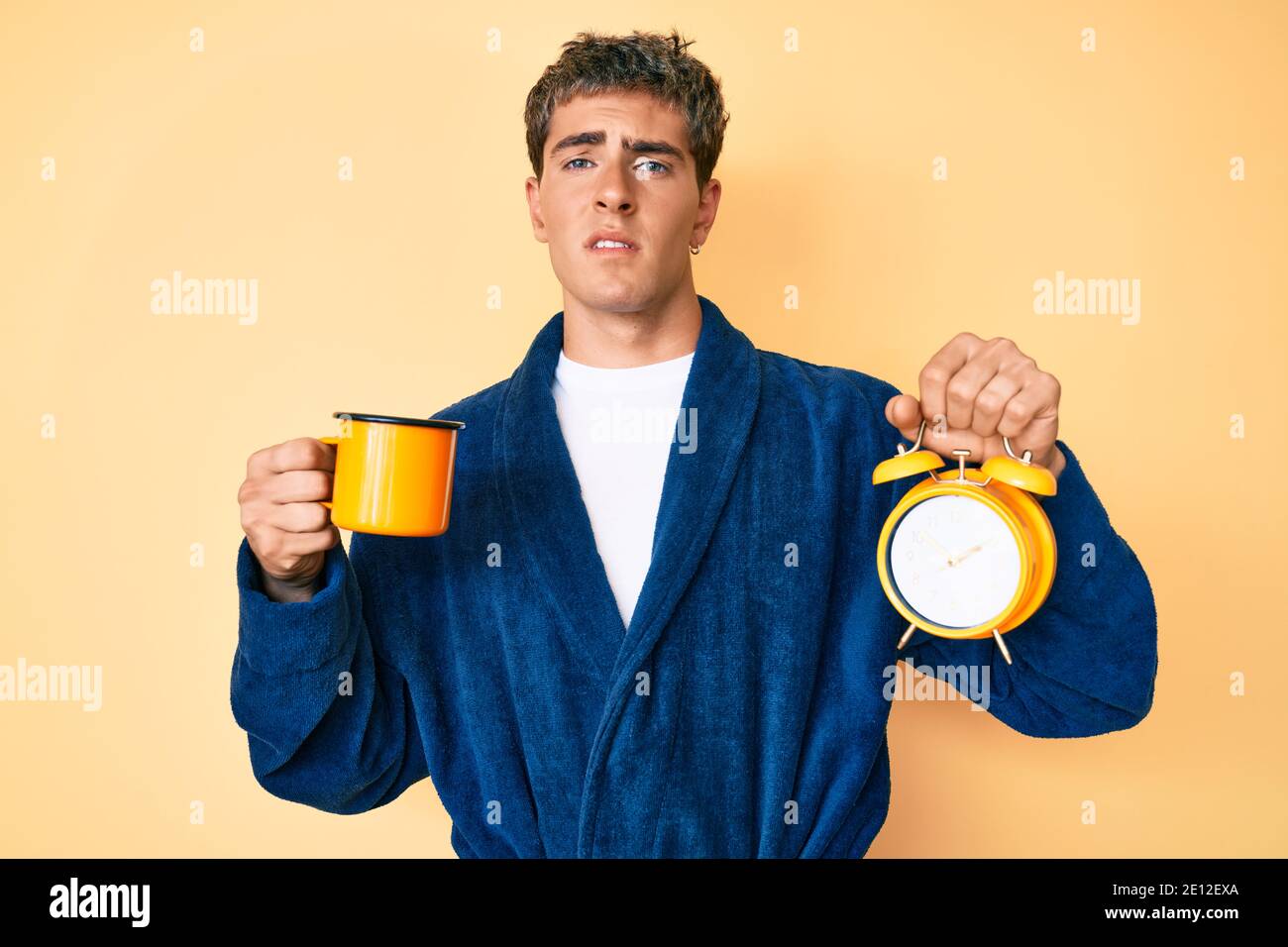 Young handsome man wearing bathrobe holding cup of coffee and alarm ...