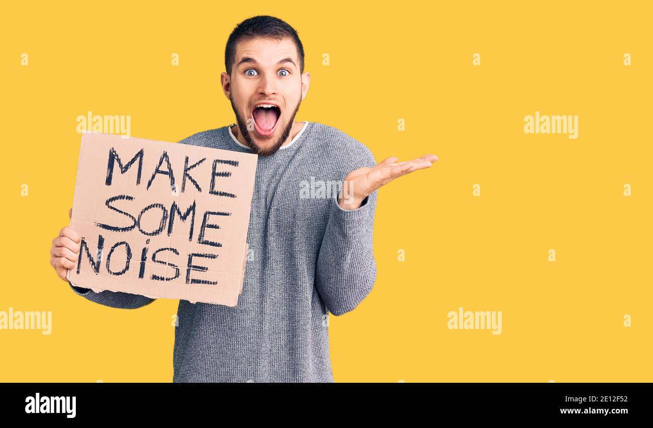 Young handsome man holding make some noise banner celebrating victory ...