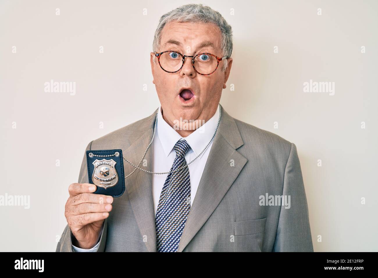 Senior grey-haired man holding detective badge scared and amazed with ...