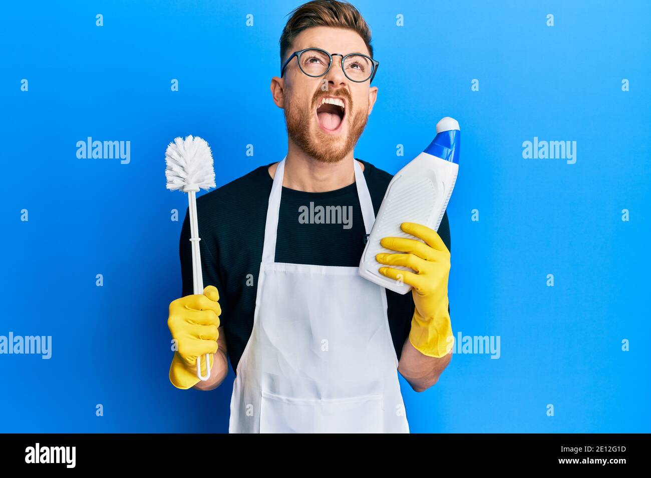 Young redhead man doing bathroom housework with toilet brush angry and ...