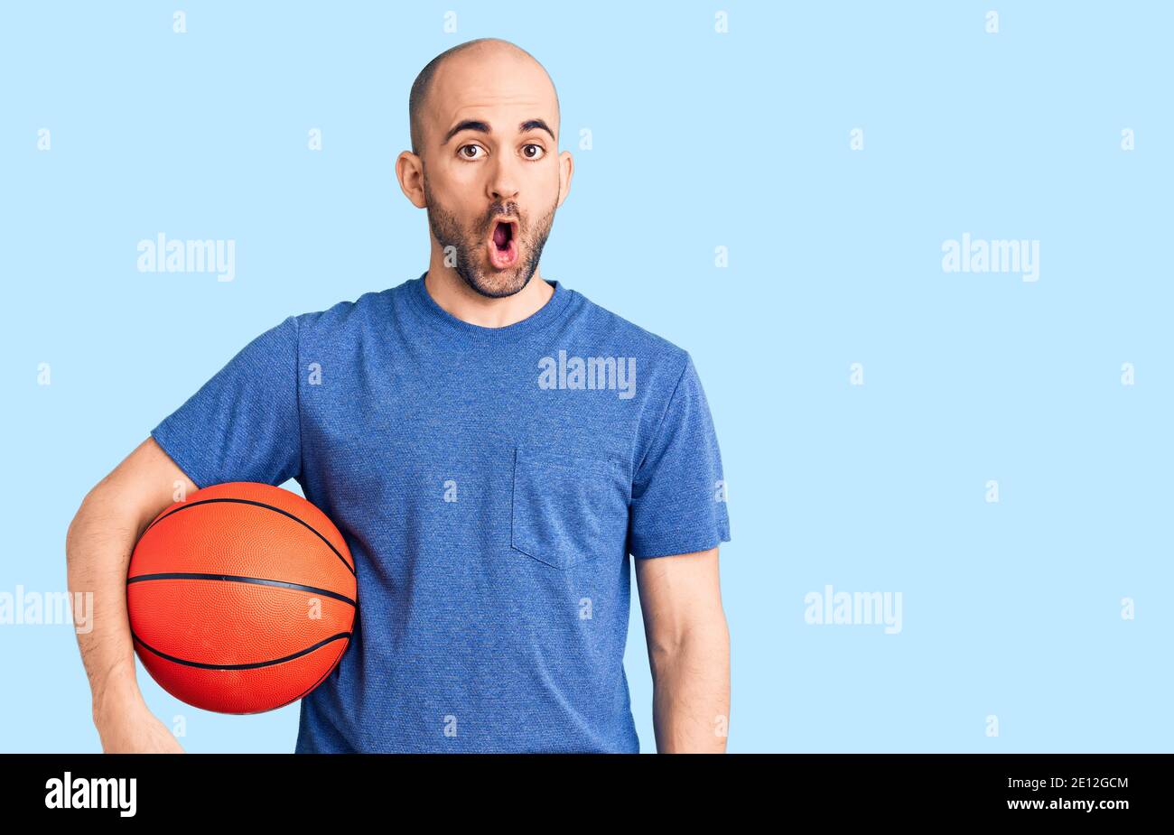Young handsome man holding basketball ball scared and amazed with open ...