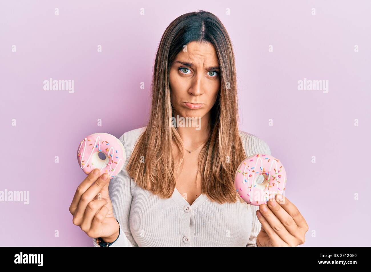 Brunette young woman holding tasty pink doughnuts depressed and worry ...
