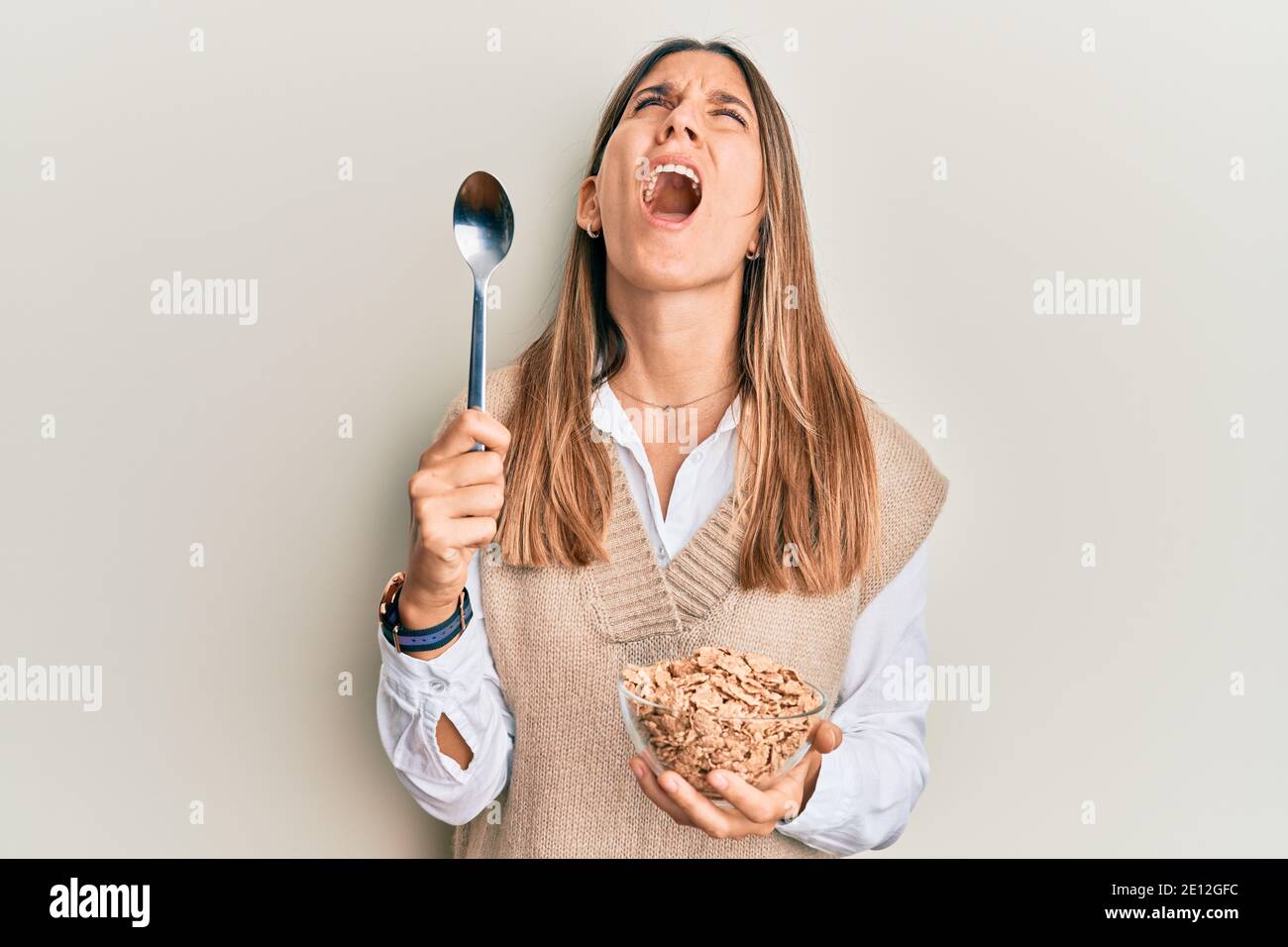 Brunette young woman eating healthy whole grain cereals with spoon ...