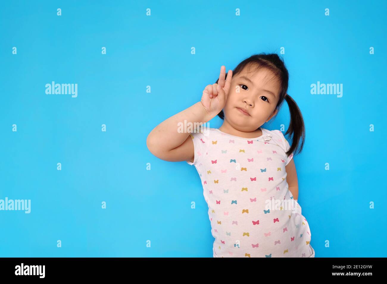 A cute young Asian girl is gesturing a victory sign using 2 fingers ...