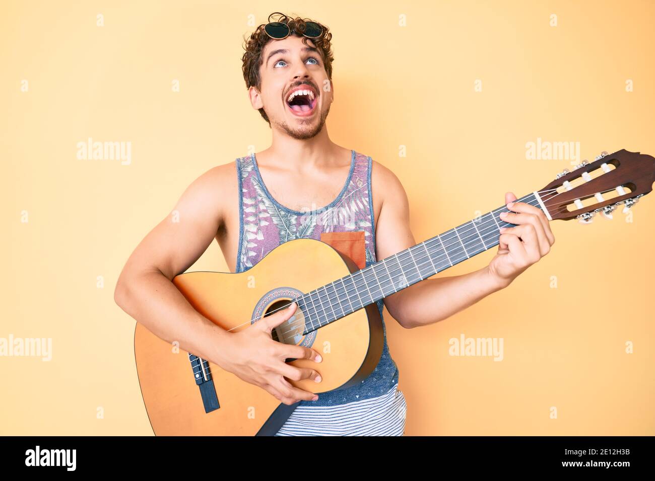 Young caucasian man with curly hair playing classical guitar angry and ...