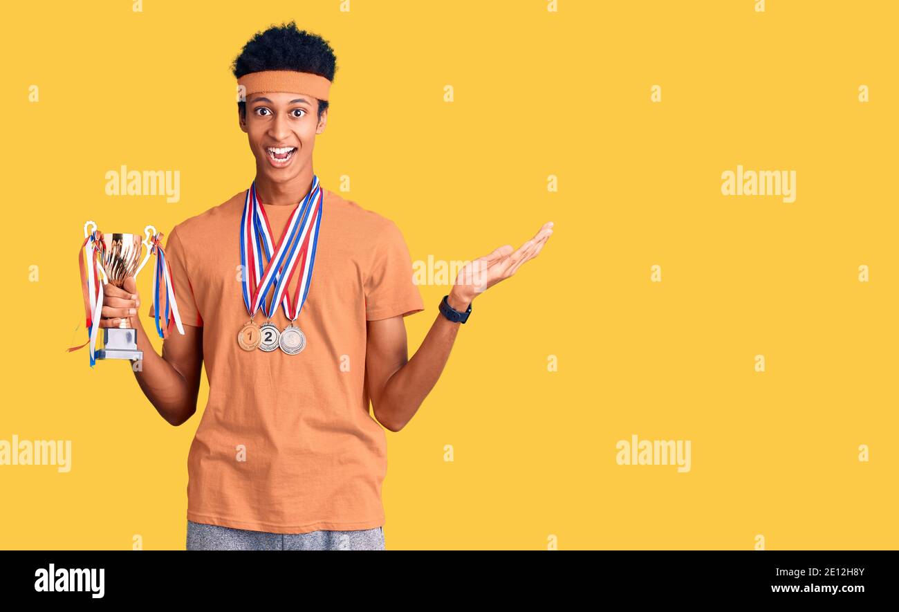 Young african american man holding champion trophy wearing medals ...