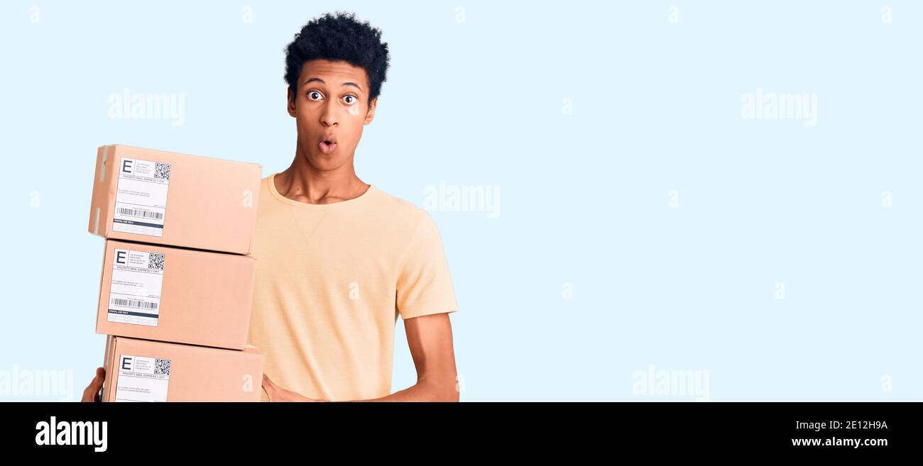 Young african american man holding delivery package scared and amazed ...