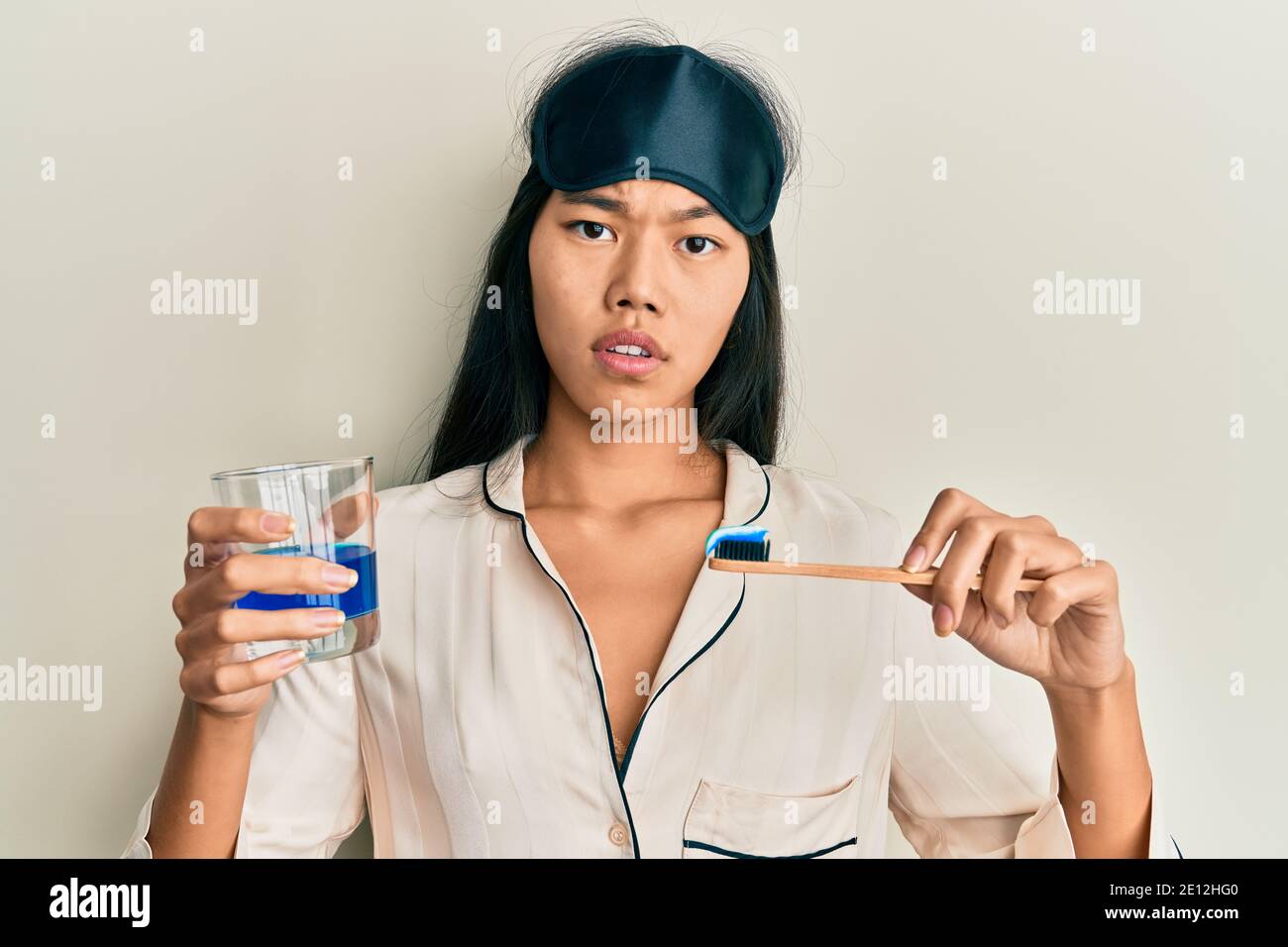 Young chinese woman wearing pajama using toothbrush and mouthwash ...