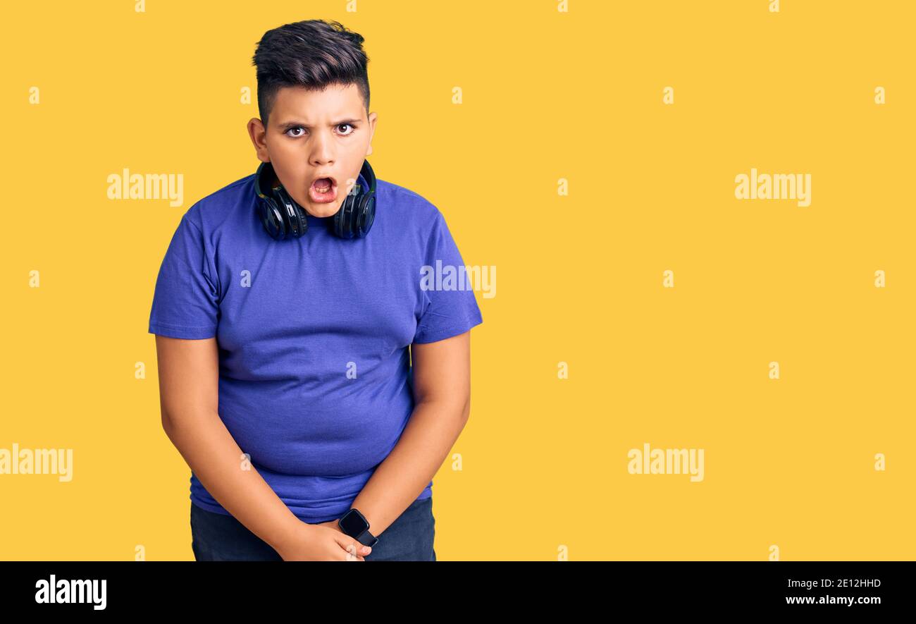 Little boy kid listening to music wearing headphones afraid and shocked ...