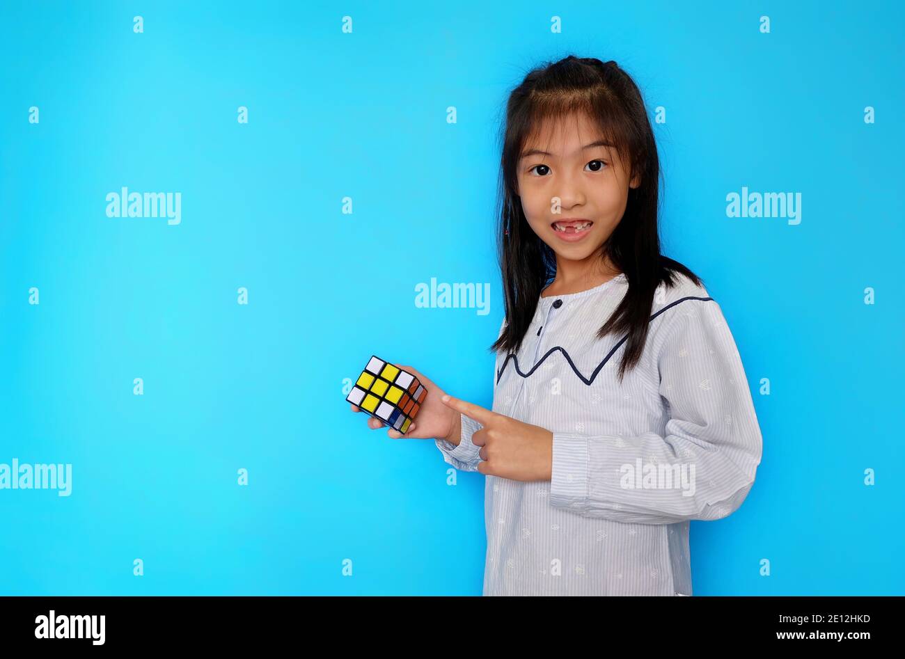 A cute young Asian girl is playing with a Rubik's cube, having fun ...