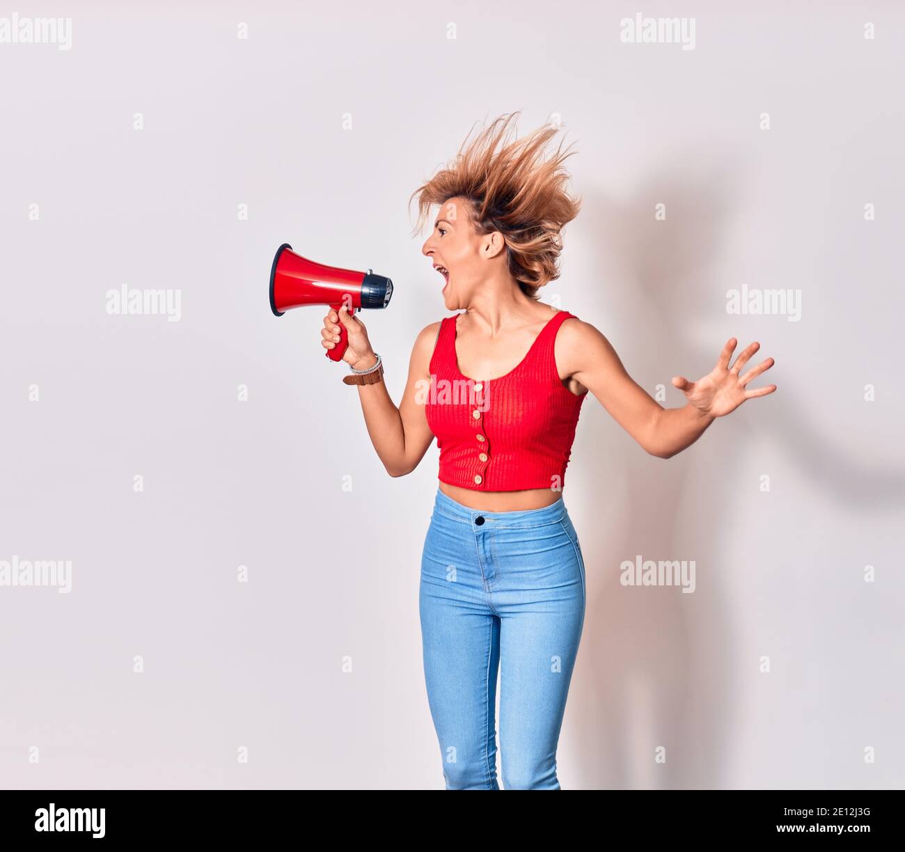 Young beautiful caucasian woman screaming using megaphone. Jumping over ...