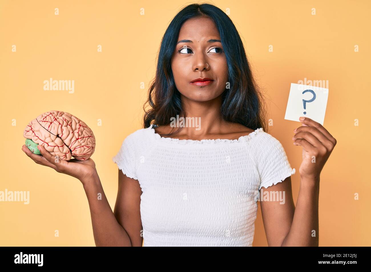 Young indian girl holding brain and question mark reminder smiling ...