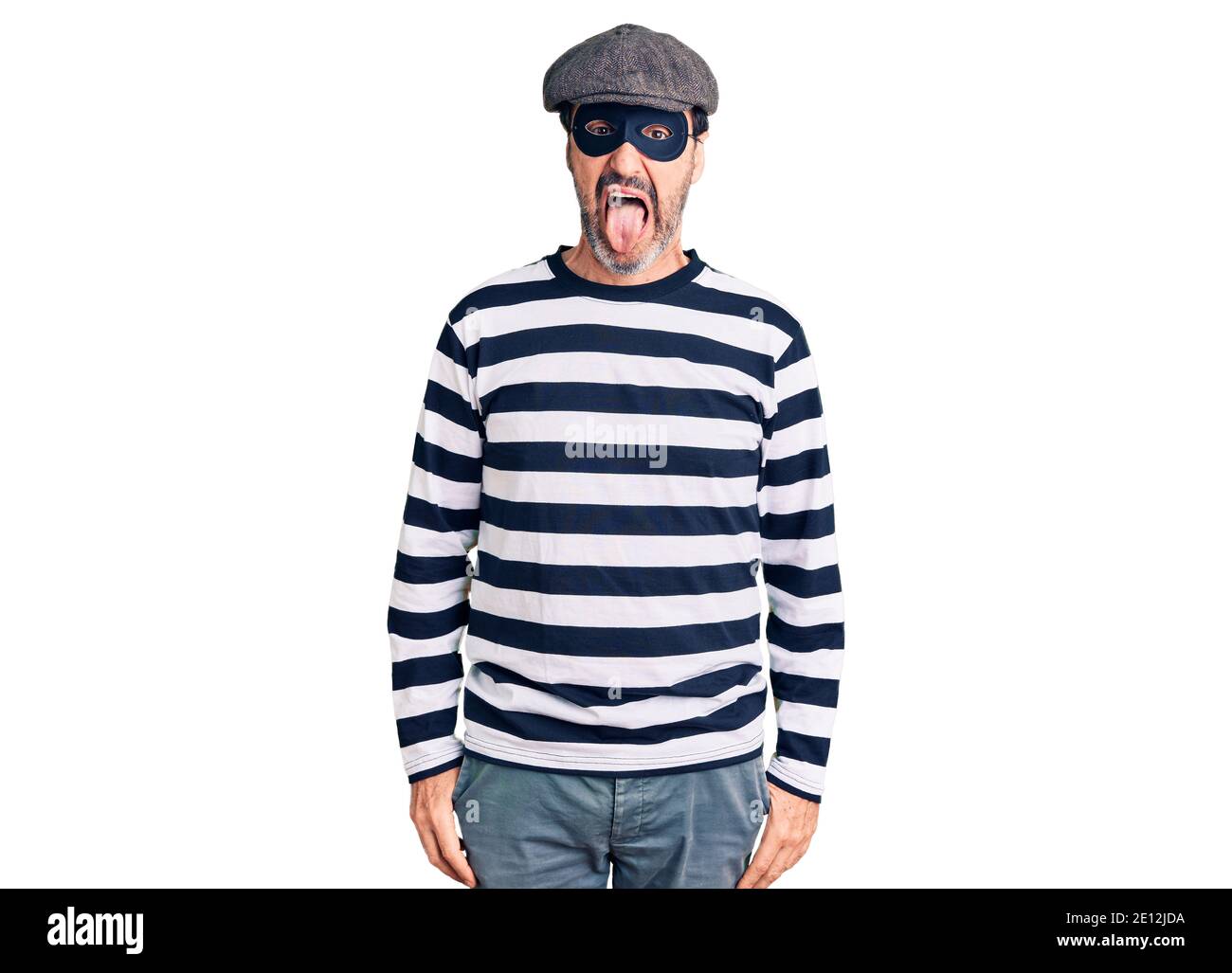 Middle age handsome man wearing burglar mask sticking tongue out happy ...