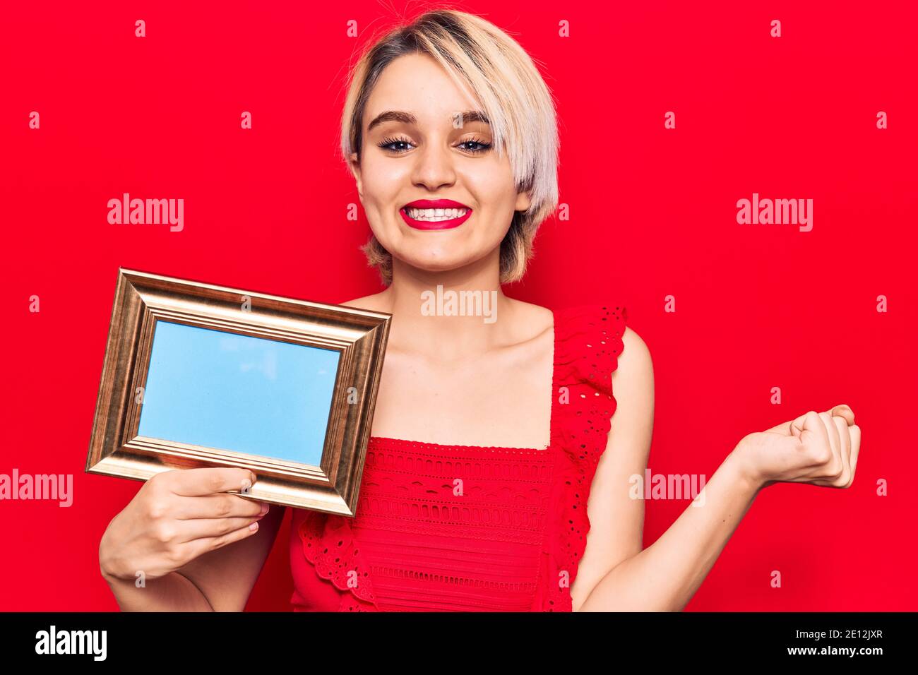 Young beautiful blonde woman holding empty frame screaming proud ...