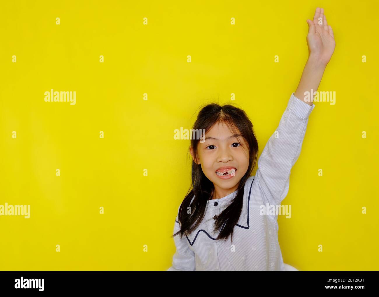 A cute young intelligent Asian girl excitedly raising her hand to ...