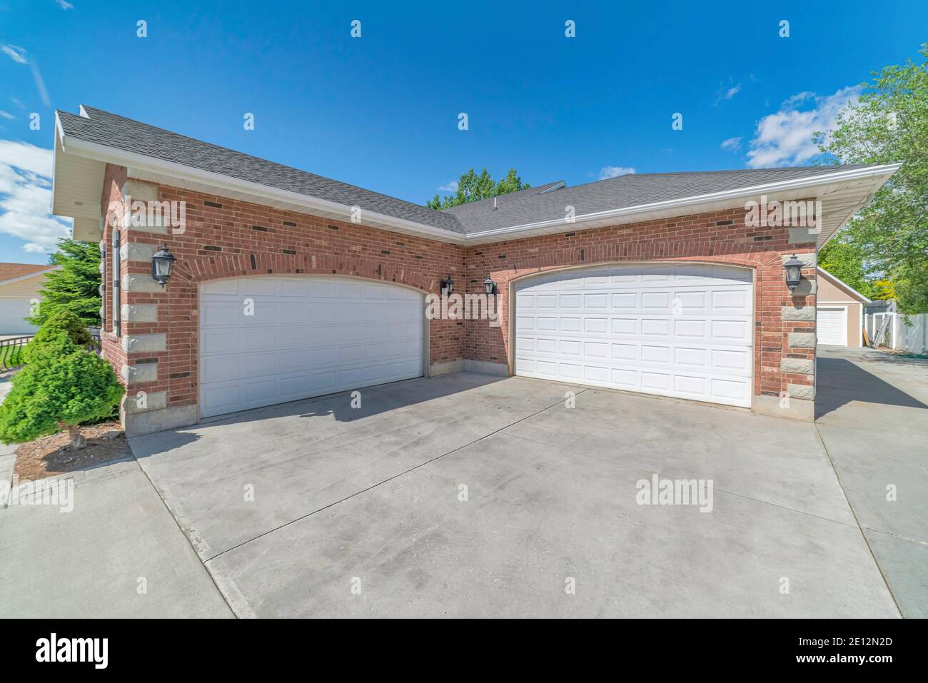 Garage with two arched white doors and red brick wall against sunny ...