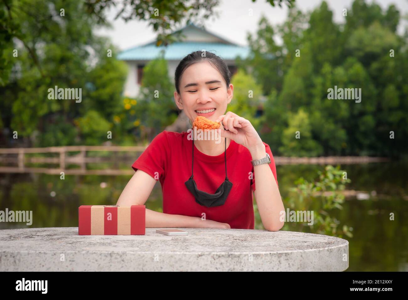 Asian women eating chicken wing sitting on table Stock Photo - Alamy