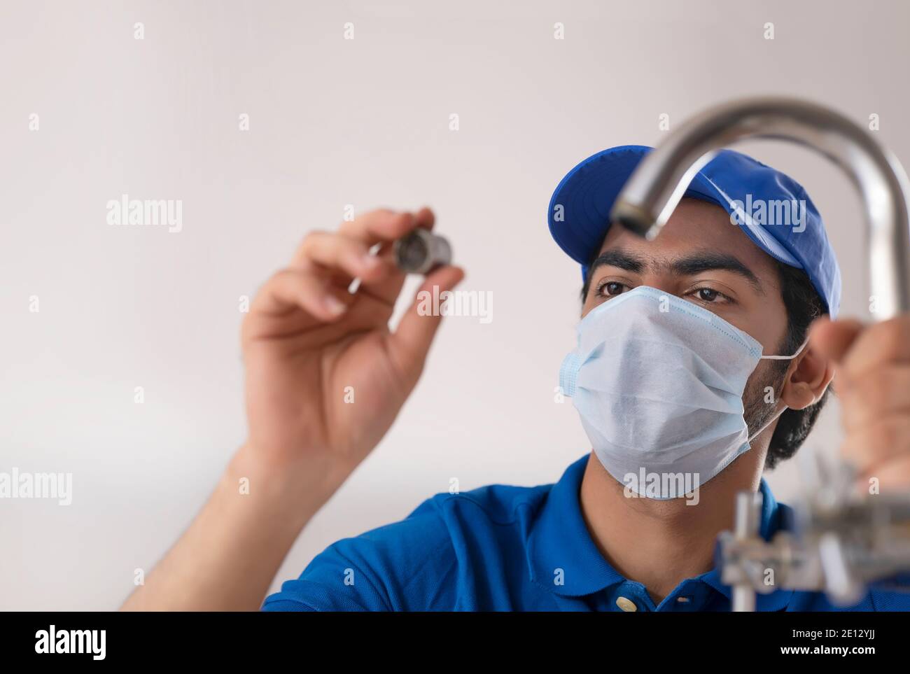A PLUMBER WEARING FACE MASK HOLDING BROKEN PART OF A PIPE WHILE WORKING ...