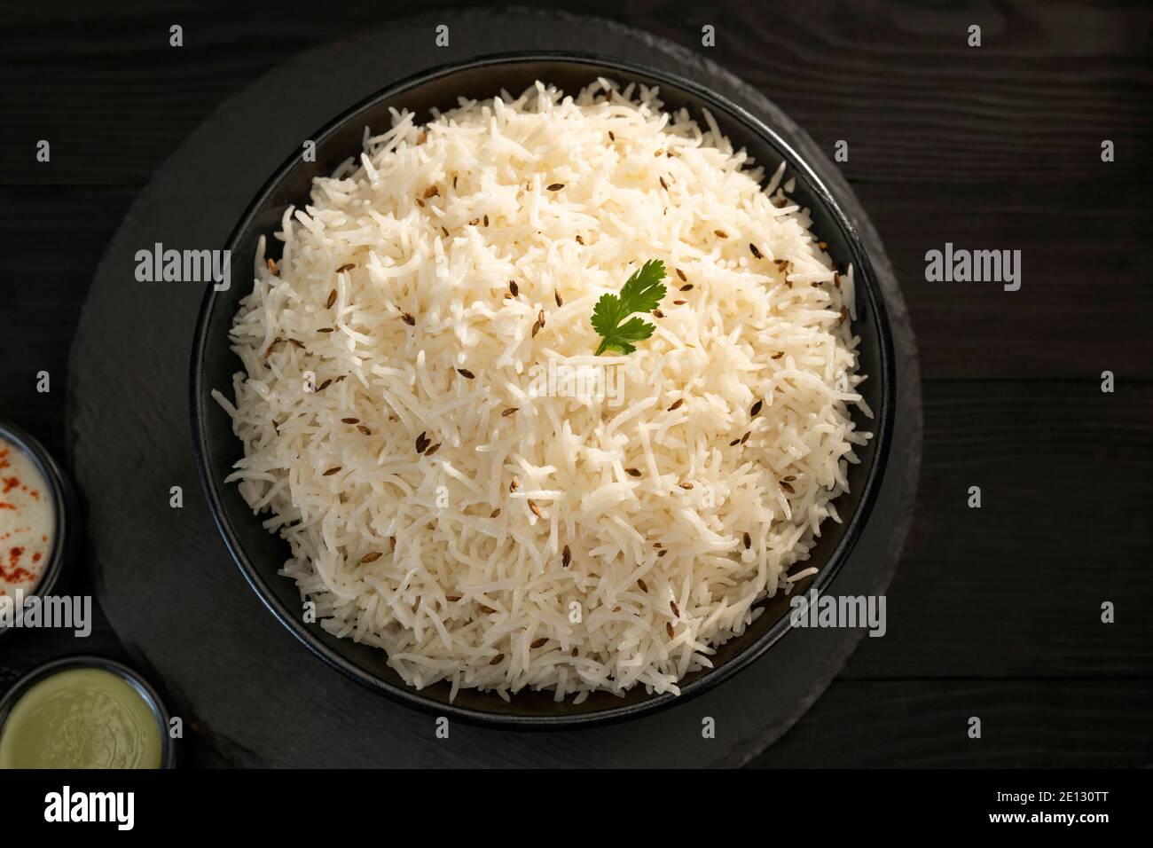 Steamed rice with Cumin in a black bowl with green chutney and curd ...